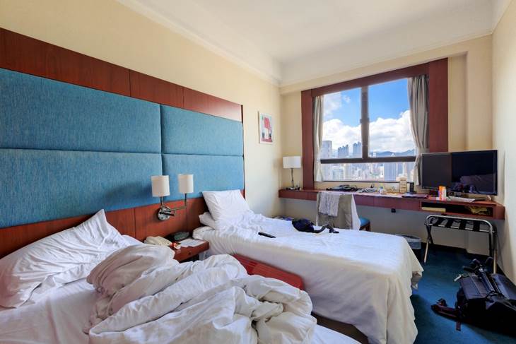 Messy hotel room with two full sized beds. One bed is left unmade ...